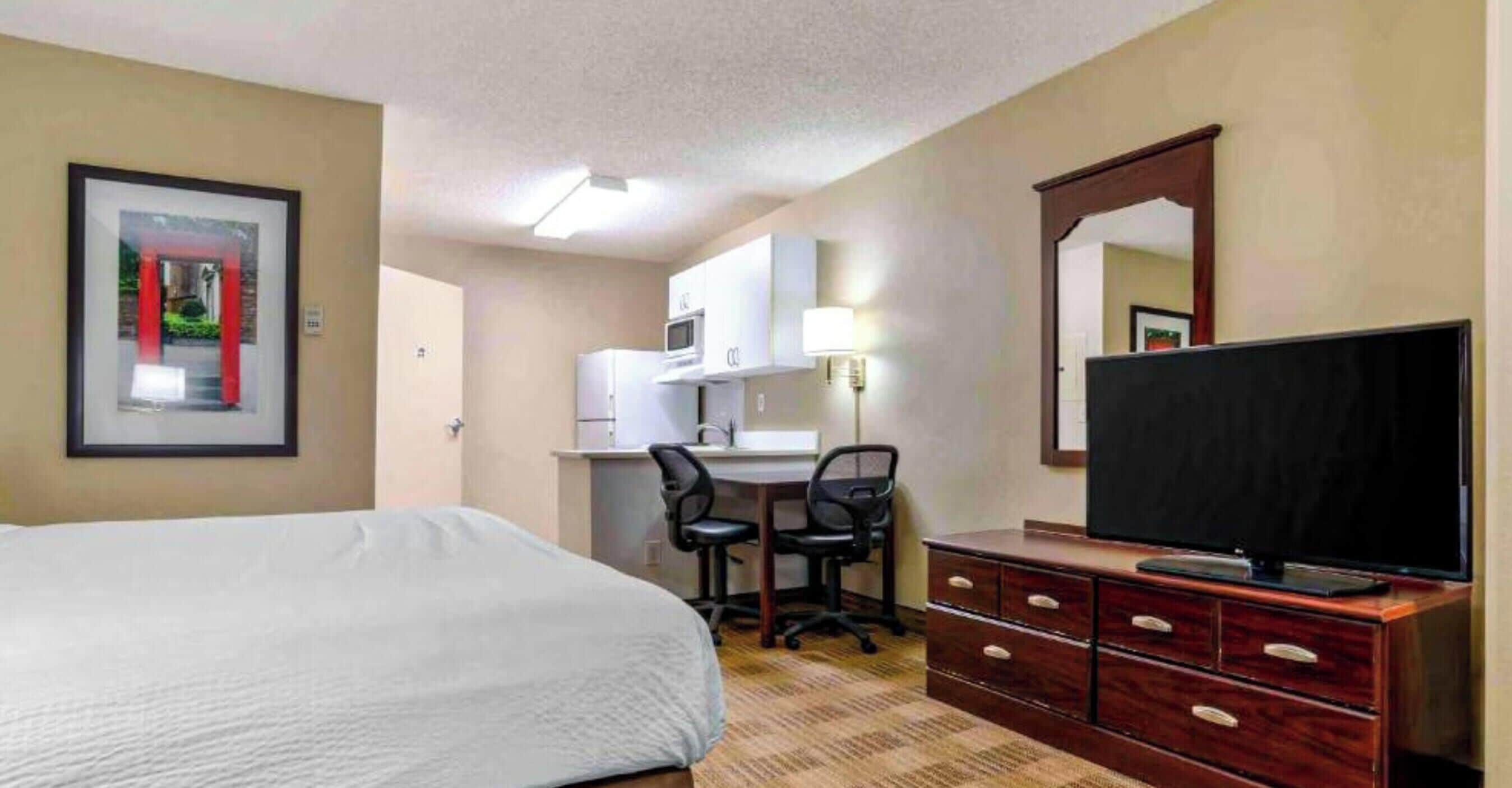 Quarto de hotel com cama, escrivaninha, cadeira de escritório, televisão e cómoda.