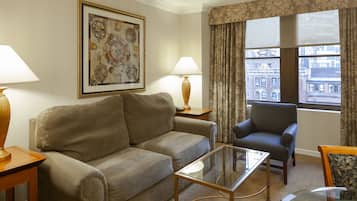 Sala de estar com sofá, poltrona, mesa de centro de vidro, luminárias e uma janela grande com cortinas.