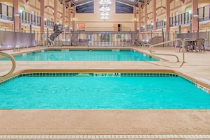Piscina interna com água cristalina, rodeada por um deck ladrilhado e um corrimão.