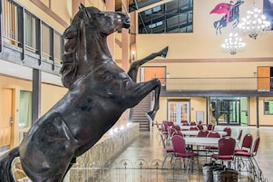 Amplo espaço interno com uma grande escultura de bronze de um cavalo, várias mesas de jantar com cadeiras vermelhas e um lustre.