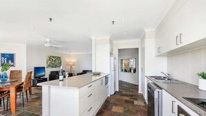 Uma cozinha moderna com armários brancos, uma ilha central e uma área de jantar com mesa e cadeiras.