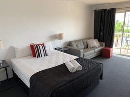 Quarto de hotel com cama, sofá, mesinha e janela com cortinas.
