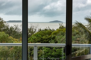 Vista da janela com uma paisagem de águas e terras distantes, tudo envolto em vegetação exuberante.