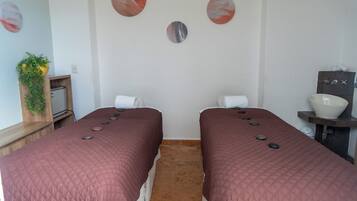 Quarto com duas camas, uma pequena escrivaninha de madeira, um vaso com planta e uma pia fixada na parede.