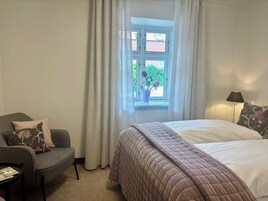 Quarto com cama, cadeira, luminária e janela com cortinas.
