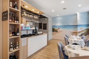 Interior de restaurante com área de bar, garrafas de vinho e um mural com cena de praia.