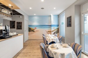 Restaurante com mural de praia, mesas preparadas para refeições e máquina de café no balcão.