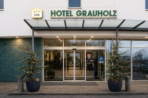 Entrada de hotel com porta de vidro, aviso de serviço 24 horas e placa de estacionamento.