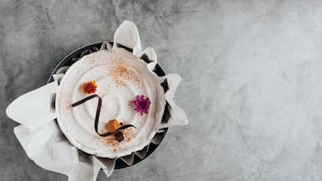 Sobremesa em um prato com um forro de papel, um raminho de flor roxa e um pedaço de chocolate por cima.