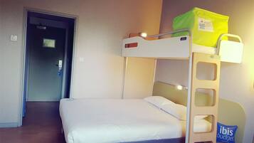Quarto com beliche, porta, luminária e travesseiro com a inscrição 'ibis budget hotels'.