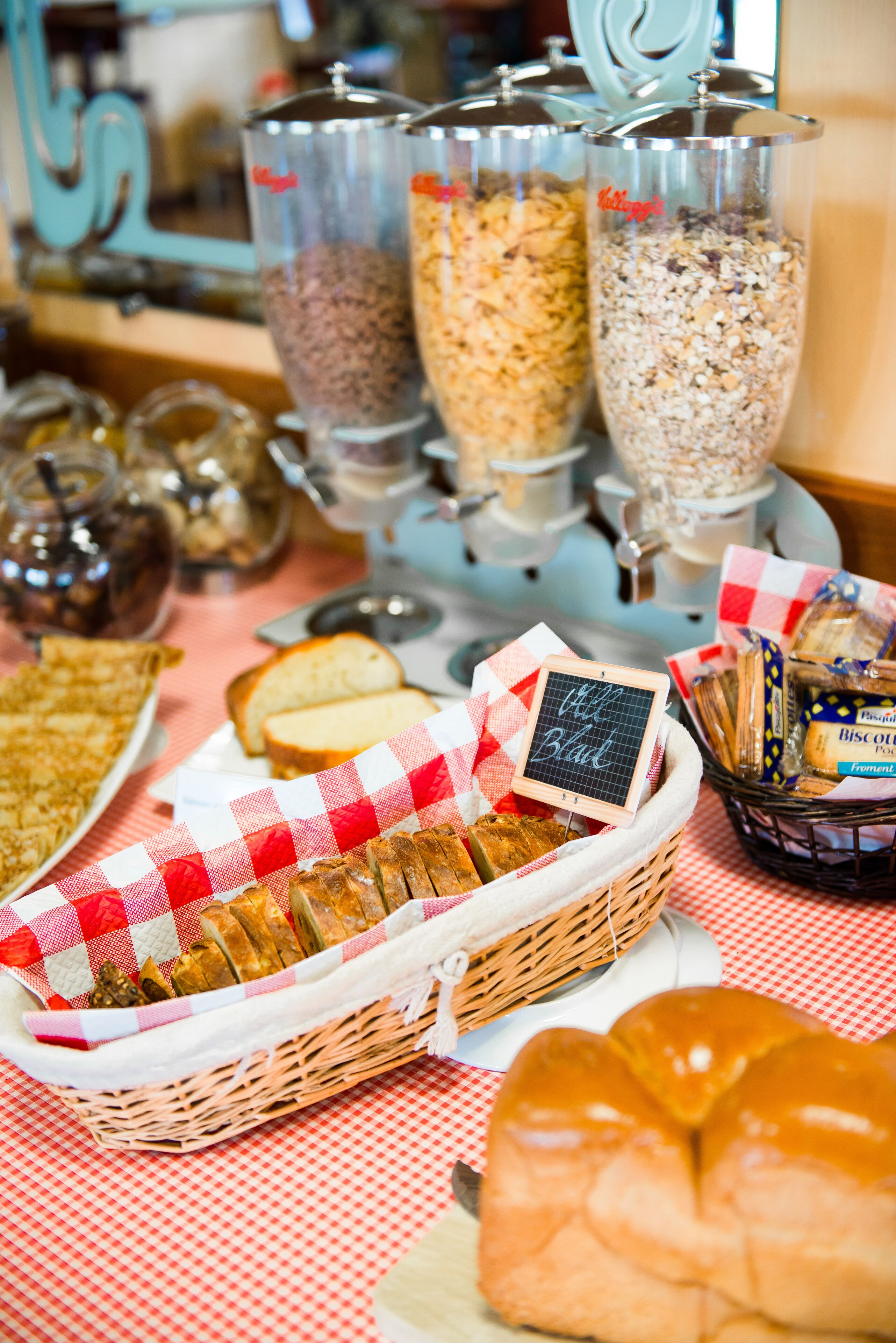 Uma mesa com diversos alimentos, incluindo pão, uma cesta de doces e recipientes com granola.