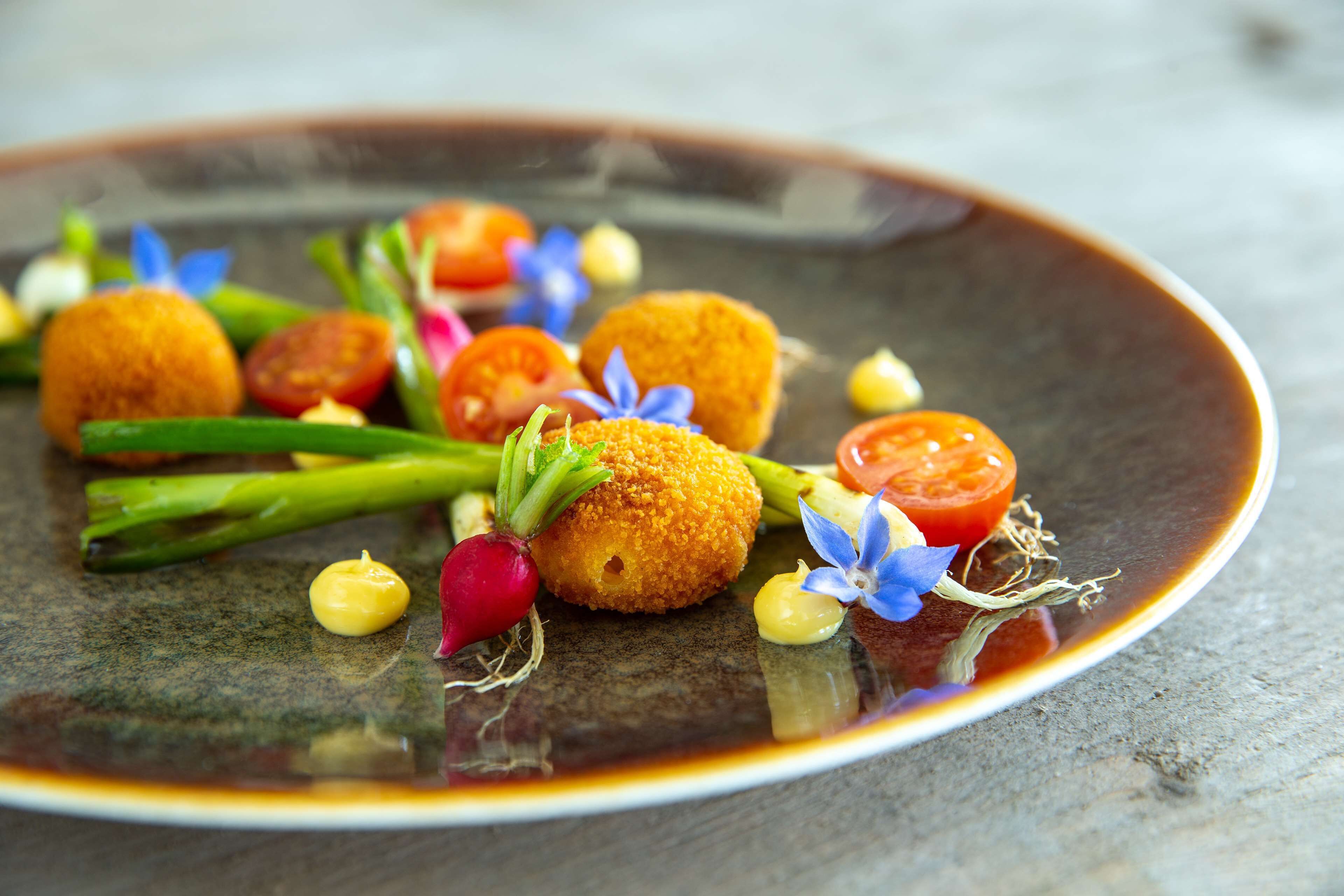 Um prato com croquetes, tomates cereja e aspargos verdes.