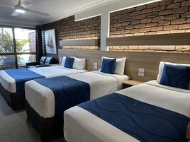 Quarto de hotel com três camas, parede de tijolos e uma janela grande.