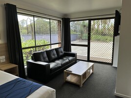 Quarto de hotel moderno com sofá de couro preto, mesa de centro de madeira e uma grande janela com vista para o exterior.
