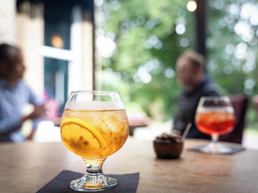 Um copo de cerveja com uma fatia de limão sobre uma mesa em um restaurante, com vista para o verde lá fora.