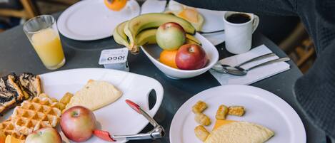 Uma mesa de café da manhã com pratos de waffles, maçãs, bananas e suco de laranja.