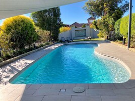 Piscina com borda curva, cercada por um deck pavimentado e uma cerca.