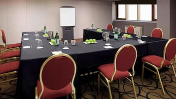 Uma sala de conferências com uma mesa comprida, cadeiras vermelhas, uma tela de projetor e vários objetos sobre a mesa.