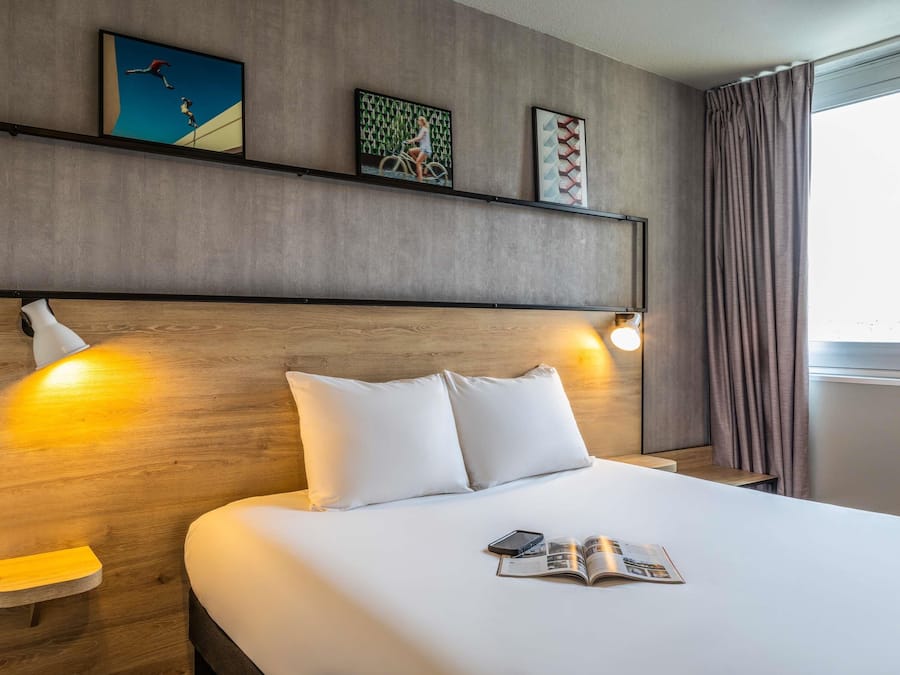 Quarto de hotel com uma cama grande, cabeceira de madeira e obras de arte na parede.