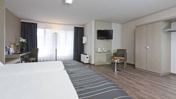 Quarto de hotel com uma cama grande, uma escrivaninha com cadeira, uma pequena mesa com cadeira, uma televisão na parede e um guarda-roupa.