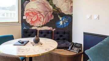 Quarto com mesa de mármore redonda, sofá estofado, pintura floral grande, telefone e janela com vista.
