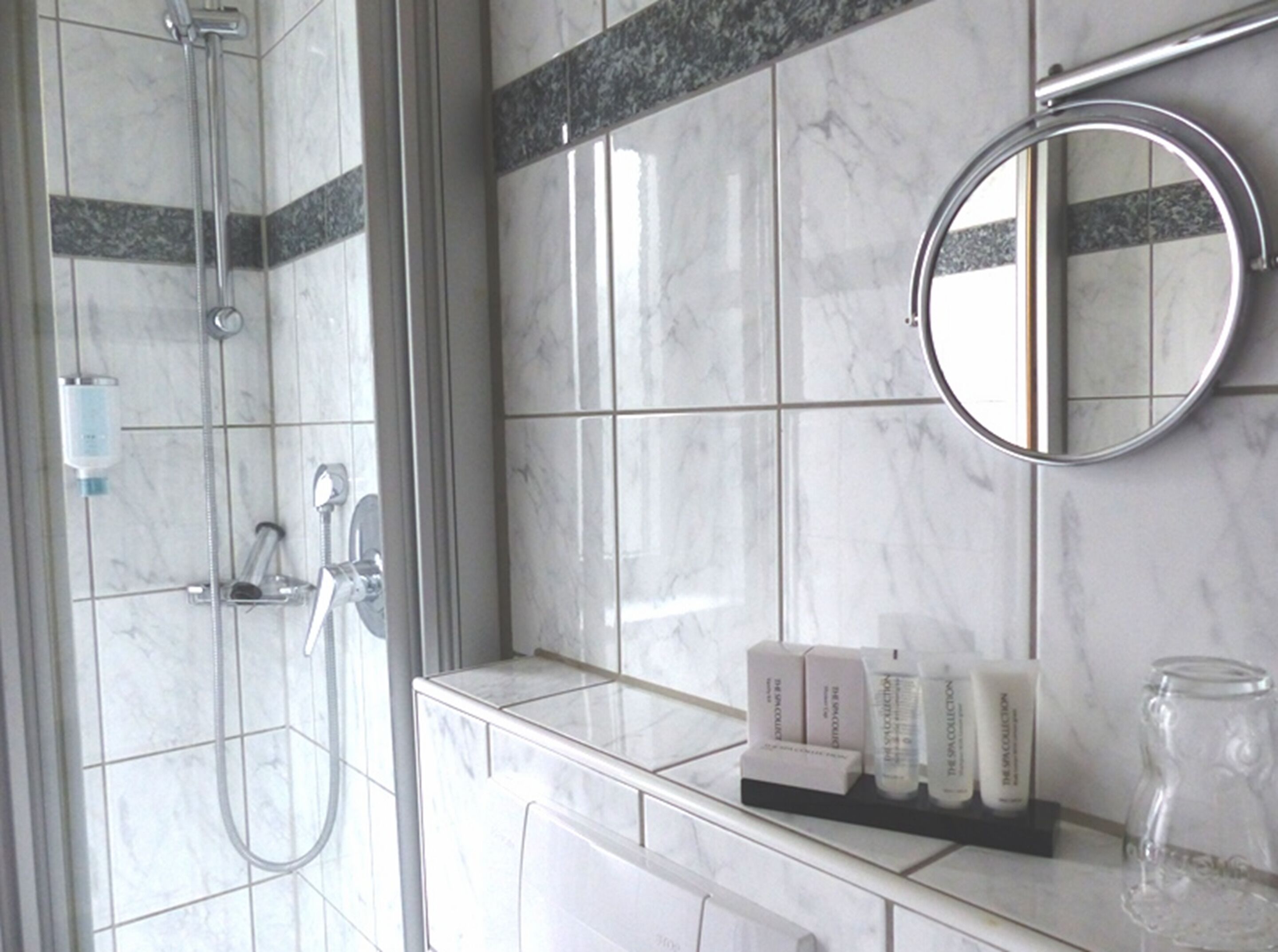 Casa de banho com chuveiro, toucador com artigos de higiene e espelho.