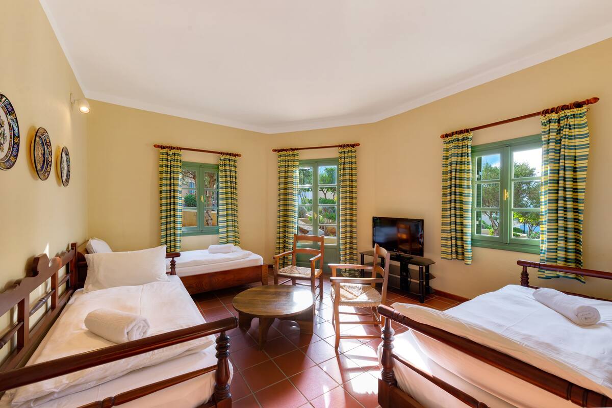 Quarto de hotel com duas camas, televisão, mesa e cadeiras.