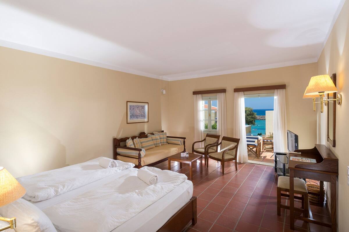 Quarto de hotel com cama, sofá, escrivaninha e vista para o mar.