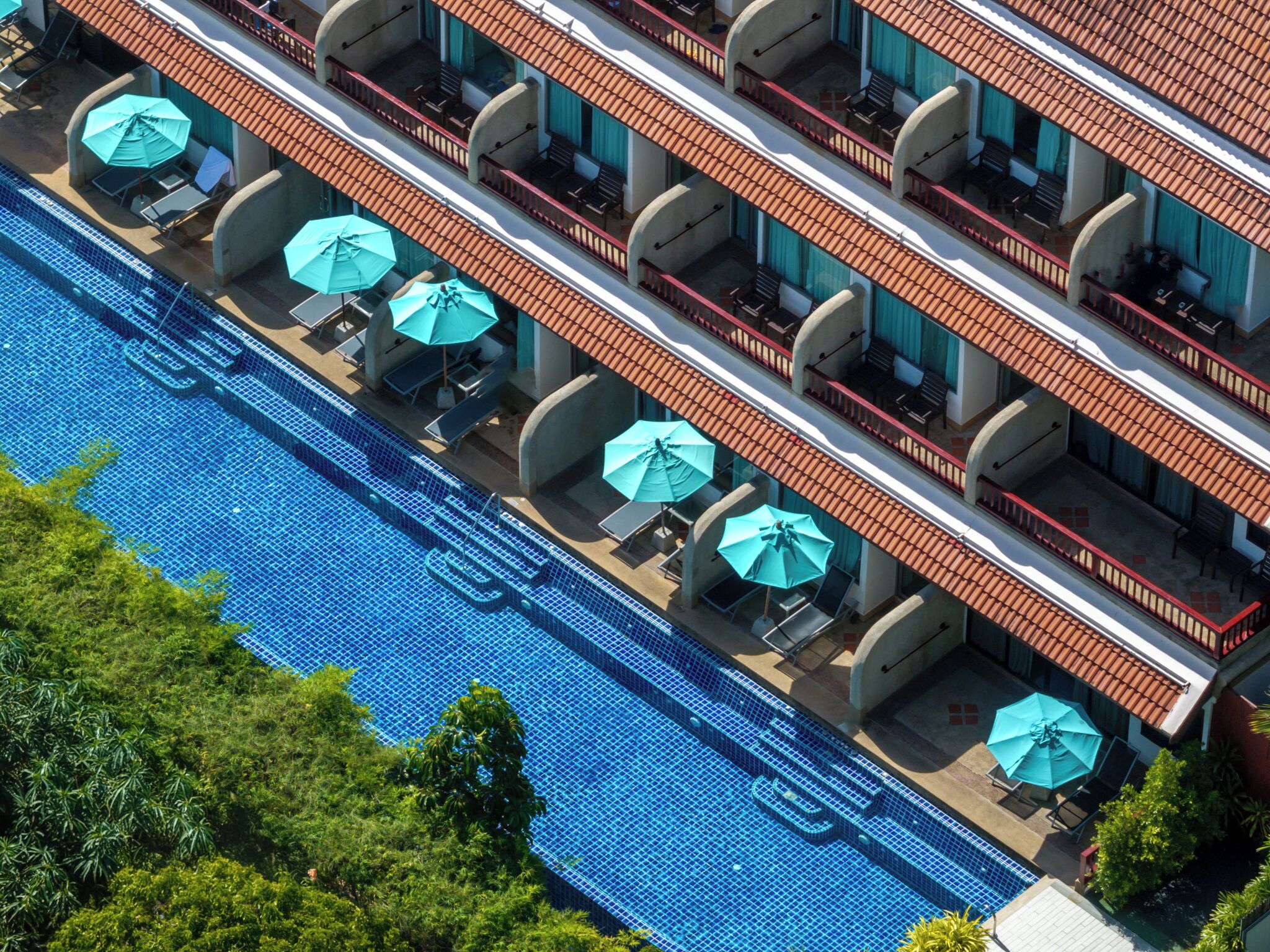 Um hotel com piscina, várias varandas e áreas de estar ao ar livre com guarda-sóis.