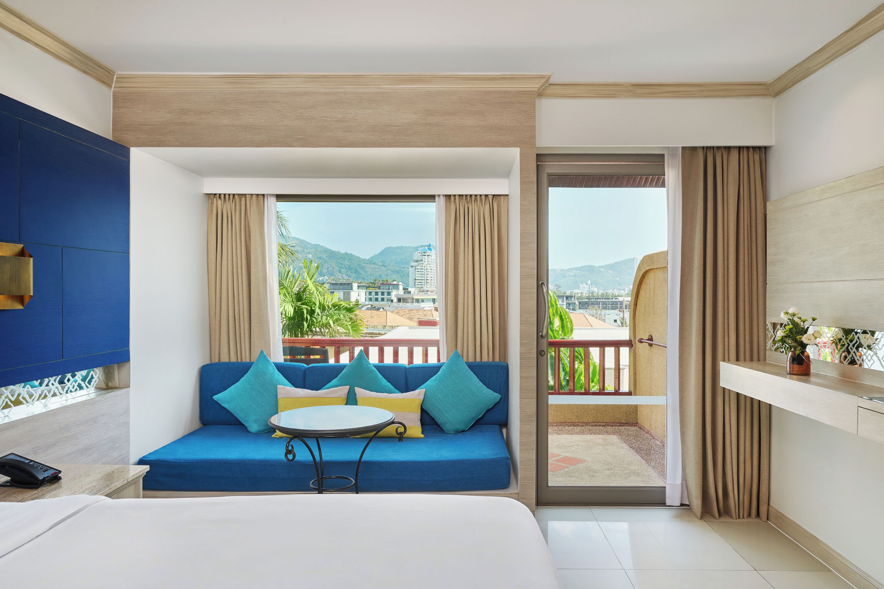 Quarto de hotel com varanda, sofá com almofadas, mesa pequena e cama.