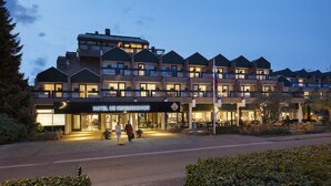 Um hotel com várias varandas, uma entrada bem iluminada e uma área de jardim ajardinada.