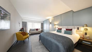 Quarto de hotel moderno com uma cama grande, um sofá, uma cadeira e uma escrivaninha.