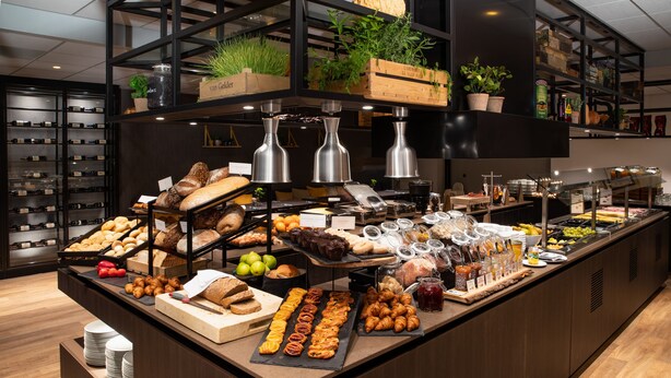 Buffet com diversos alimentos e uma estante de vinhos ao fundo.