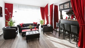 Uma sala de estar moderna com um sofá de couro preto, uma parede de destaque vermelha e um espaço bar com banquetas.