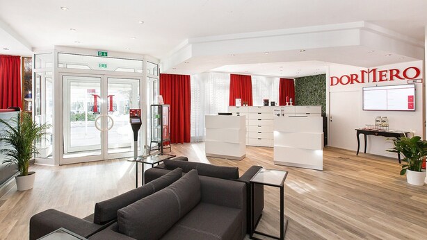 Um lobby de hotel moderno com sofá, balcão de recepção e área de kitchenette.