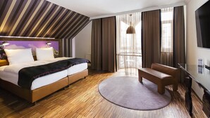 Quarto de hotel com cama, escrivaninha, cadeira, televisão e janela com cortinas.