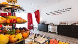 Um buffet de café da manhã com frutas e bebidas, uma frase decorativa na parede e um interior moderno.