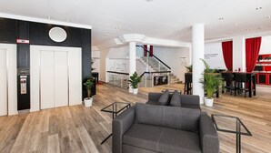 Um hall amplo com um sofá cinzento, piso de madeira, uma escada e um espaço de refeições com cortinas vermelhas.