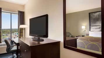 Quarto de hotel com escrivaninha, cadeira, televisão, cama e uma grande janela com vista para a cidade.