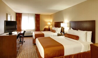 Quarto de hotel com duas camas, uma escrivaninha, televisão e luminária.