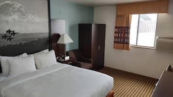 Quarto de hotel com uma cama grande, uma escrivaninha, uma cadeira, um guarda-roupa, uma janela com cortinas e um quadro na parede.