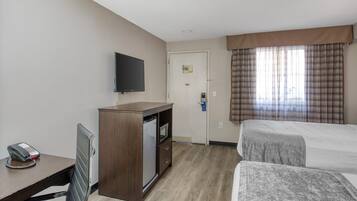 Quarto de hotel com cama, secretária com telefone, televisão e porta com placa.