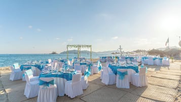 Decoração de casamento ao ar livre, com mesas e cadeiras dispostas na praia, com vista para o mar.