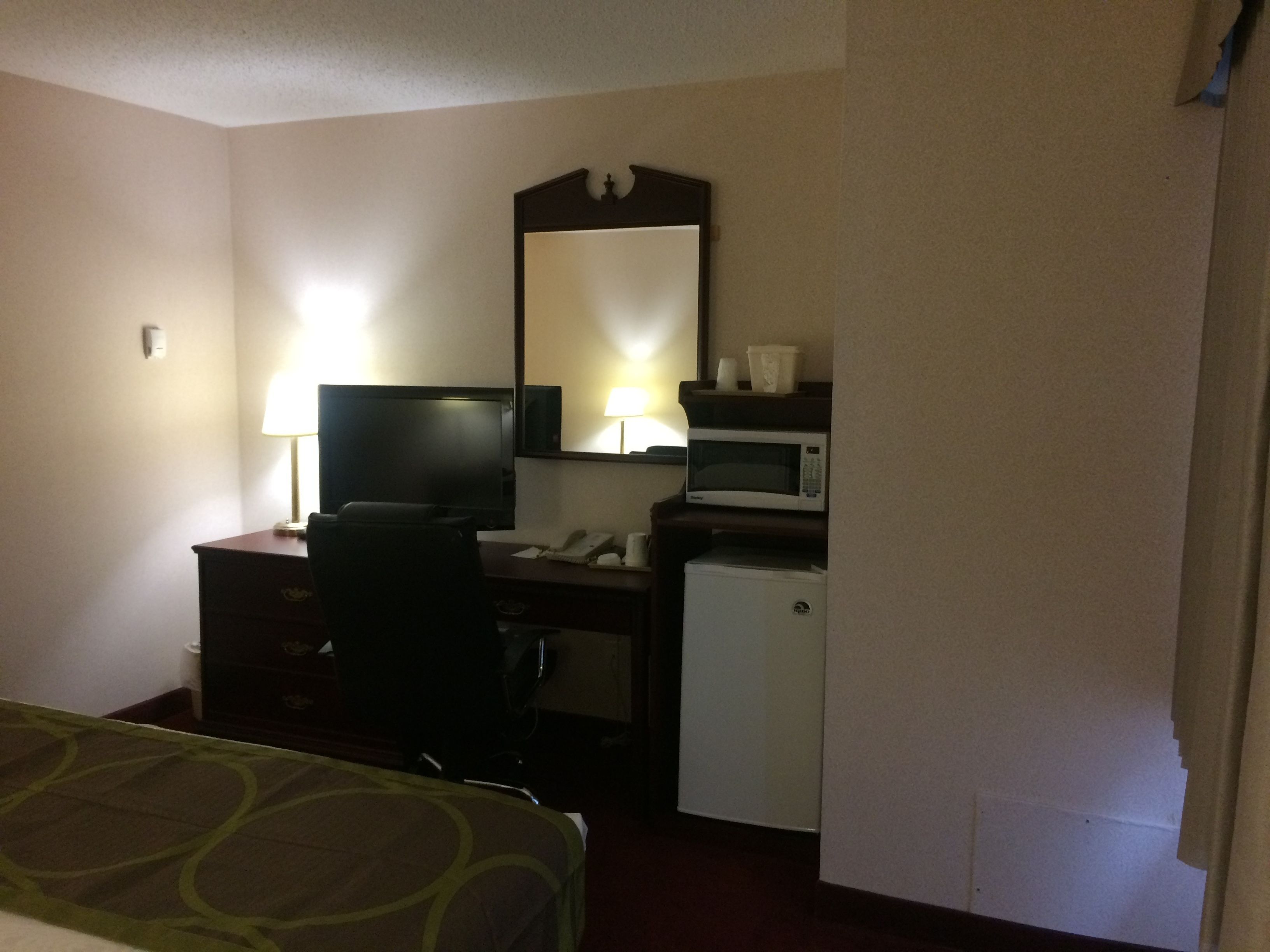 Quarto de hotel com cama, secretária com computador, micro-ondas, telefone e pequeno frigorífico.