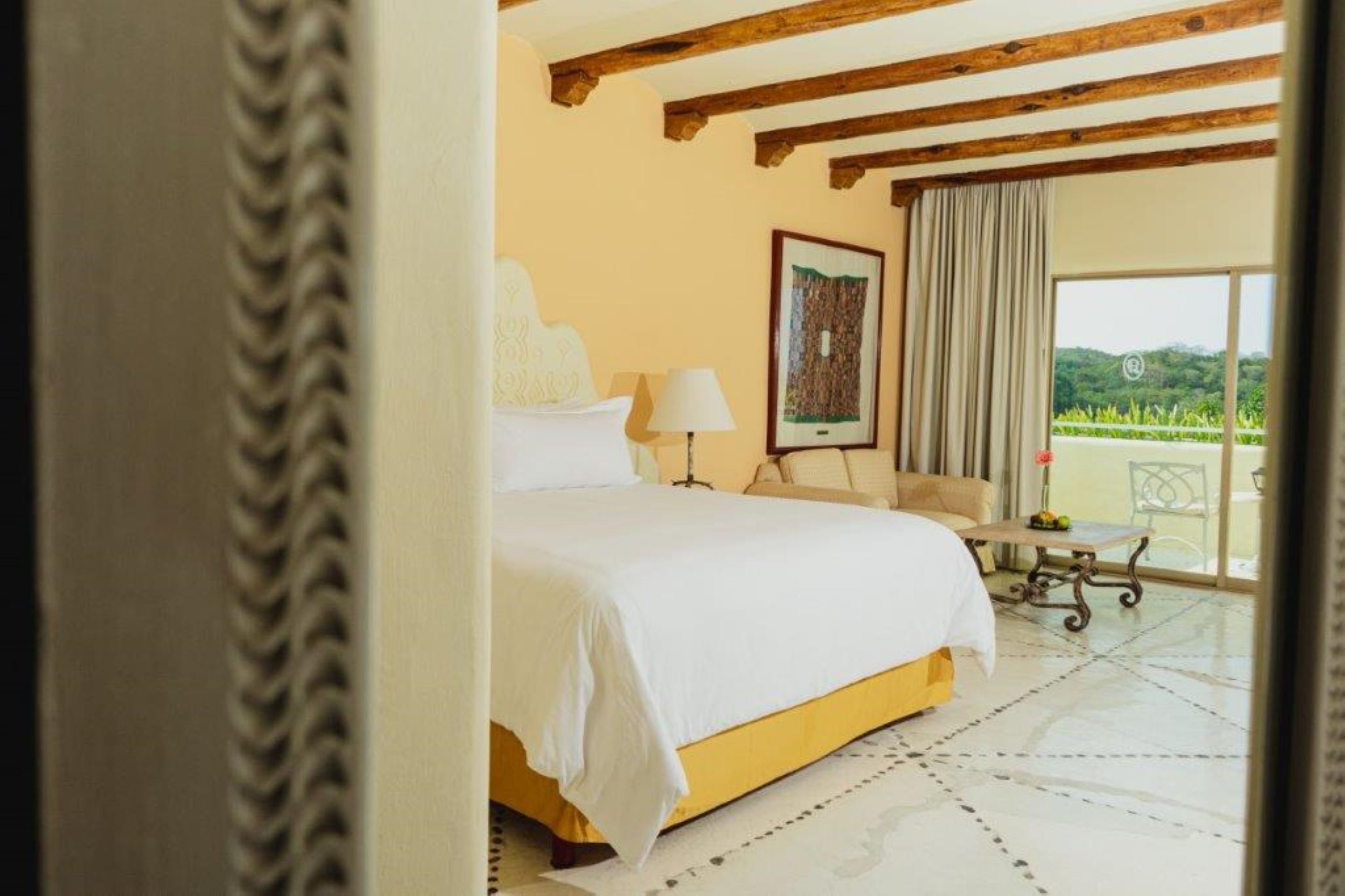 Quarto com cama, cadeira, mesa e vista para o verde lá fora.