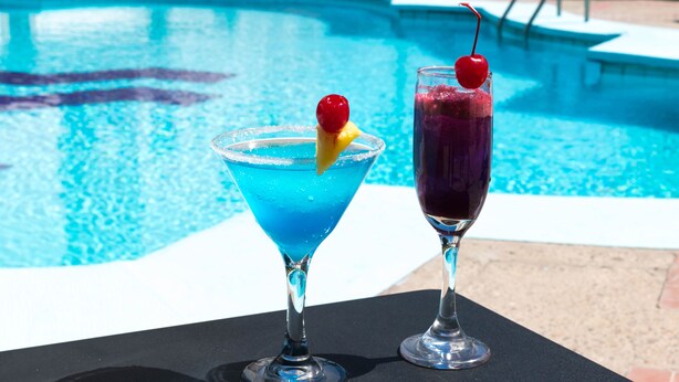 Dois cocktails com cerejas sobre uma mesa perto de uma piscina.