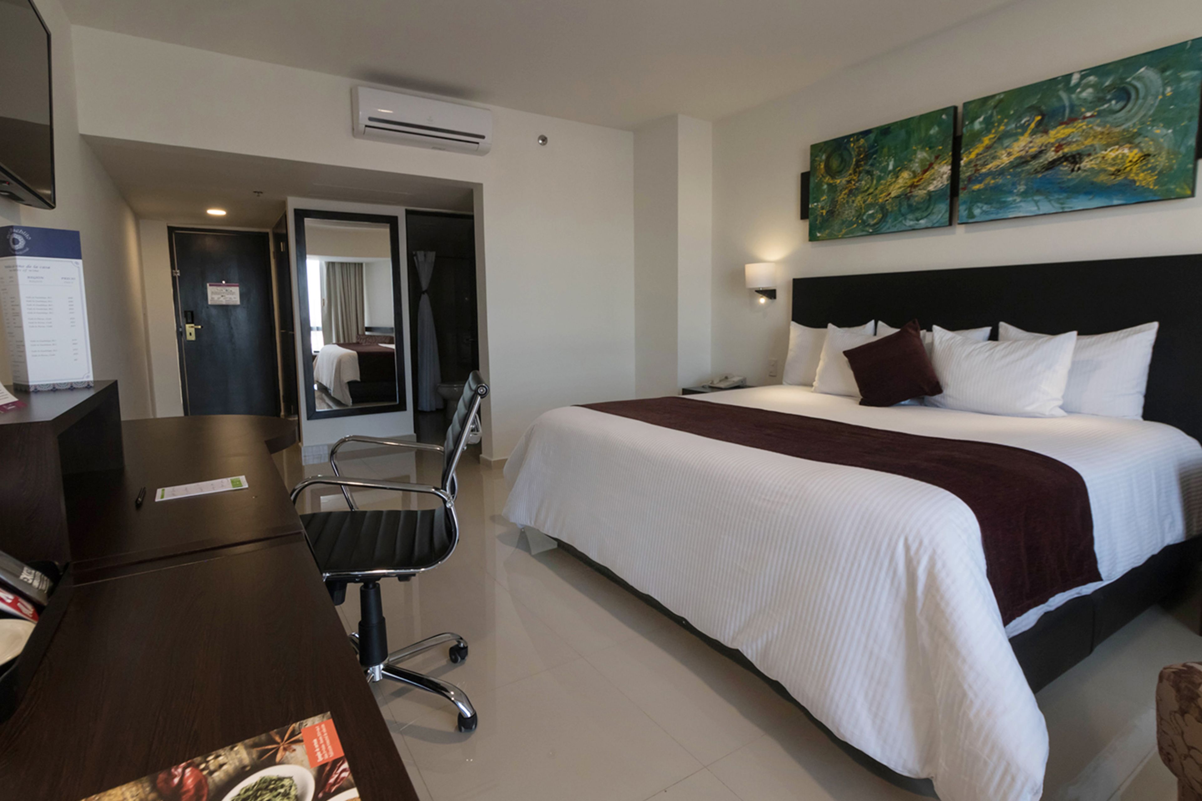 Quarto de hotel com uma cama grande, uma escrivaninha, uma cadeira e um quadro na parede.