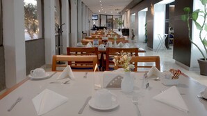 Uma sala de jantar com mesas postas para refeição, cadeiras de madeira e um vaso de planta.