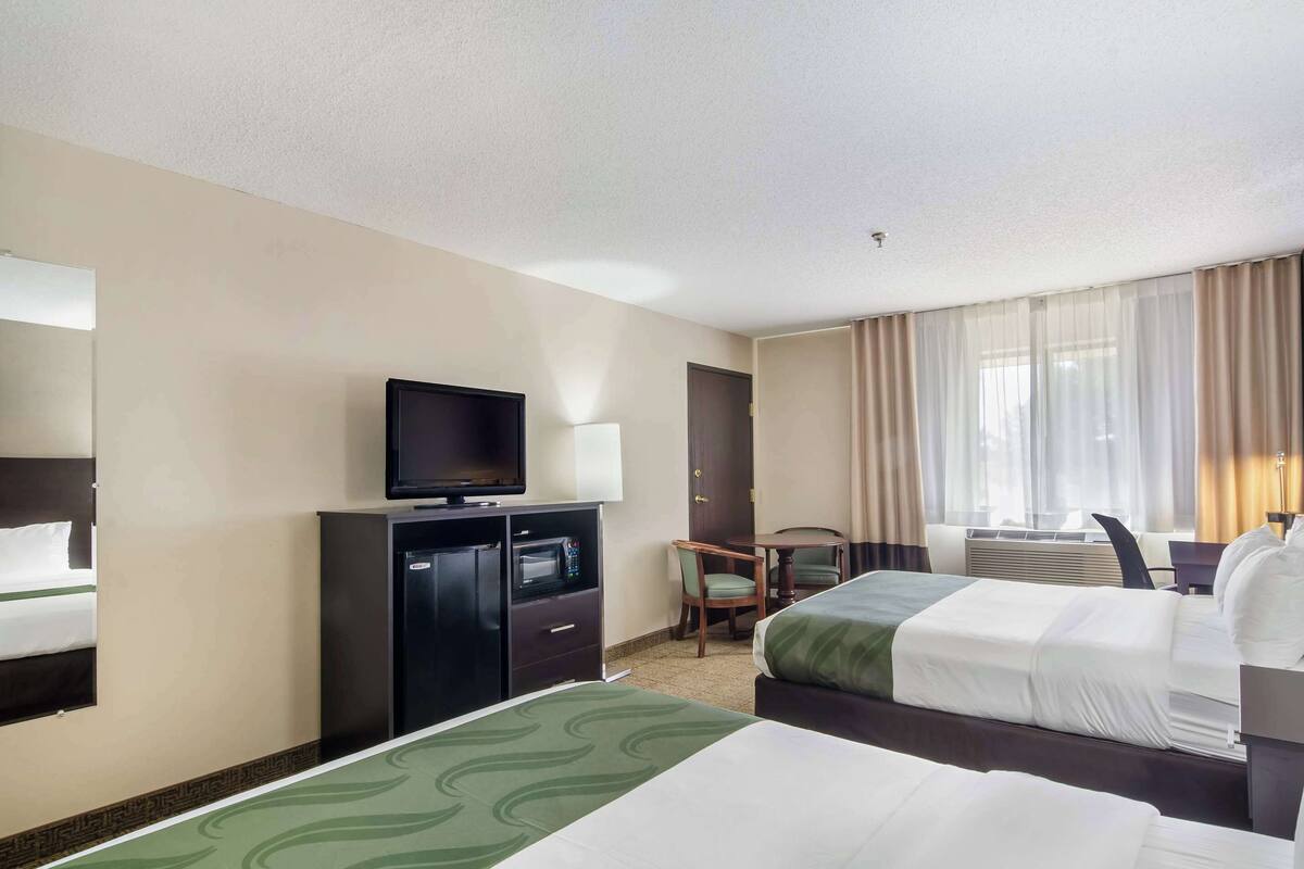 Quarto de hotel com duas camas, uma escrivaninha com cadeira, televisão e minibar.