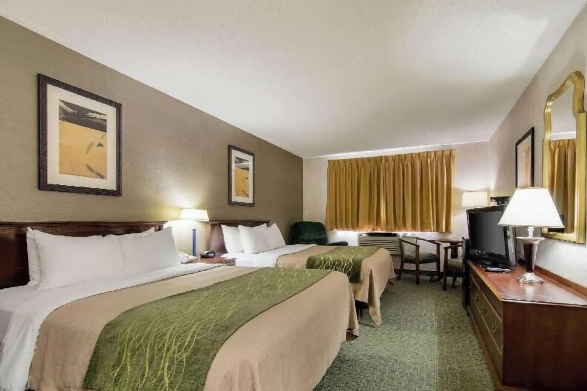 Quarto de hotel com duas camas, uma escrivaninha, uma televisão e um espelho.